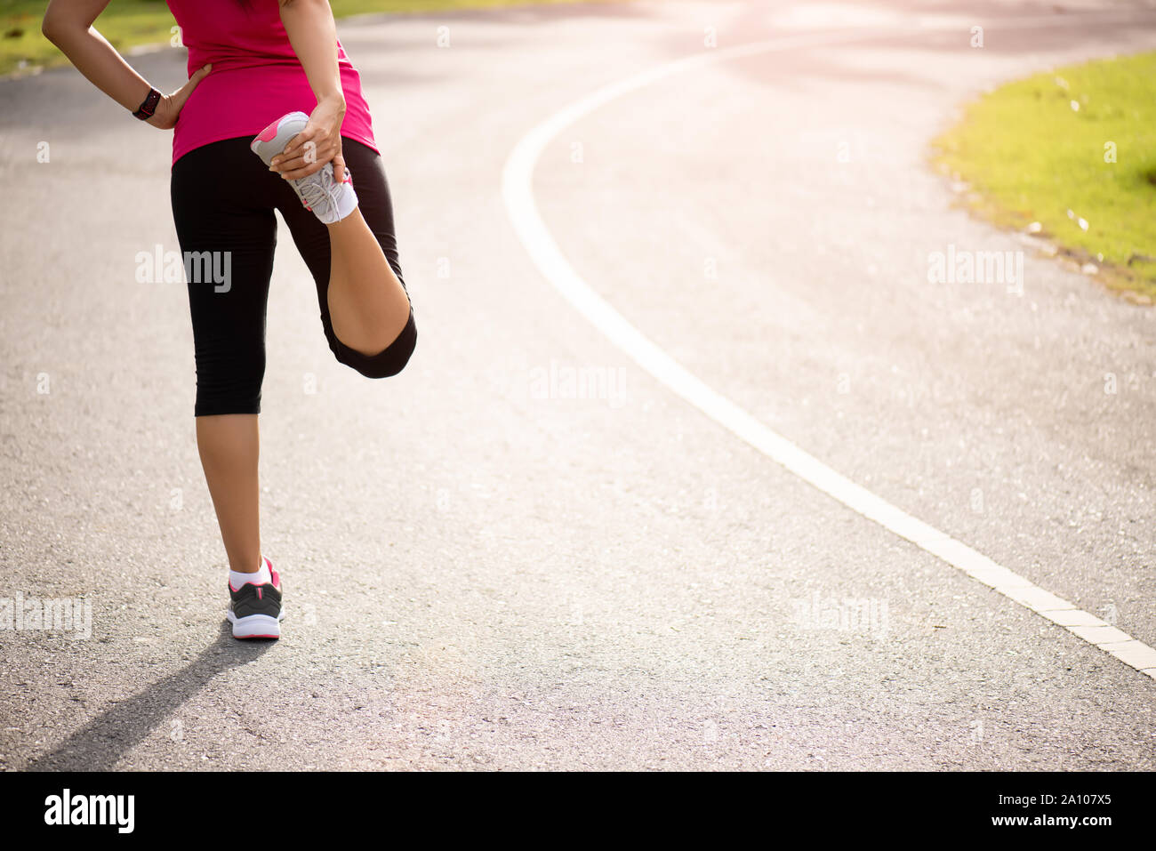 Young fitness woman runner stretching legs before run in the park. Outdoor exercise activities ...