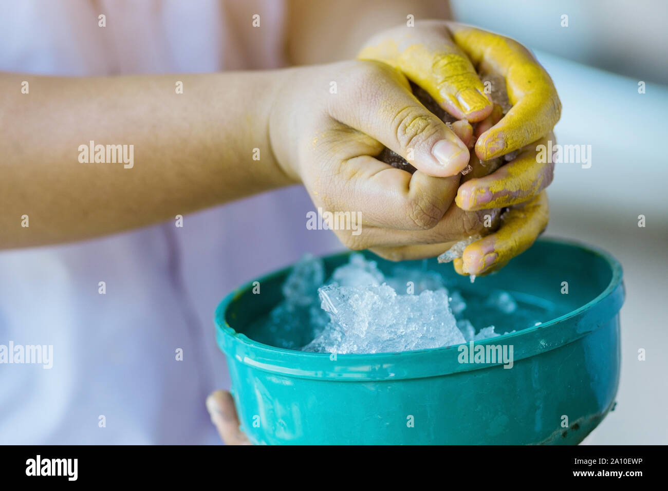 Close up to wash hands stained with yellow oil color by ice in a green ...