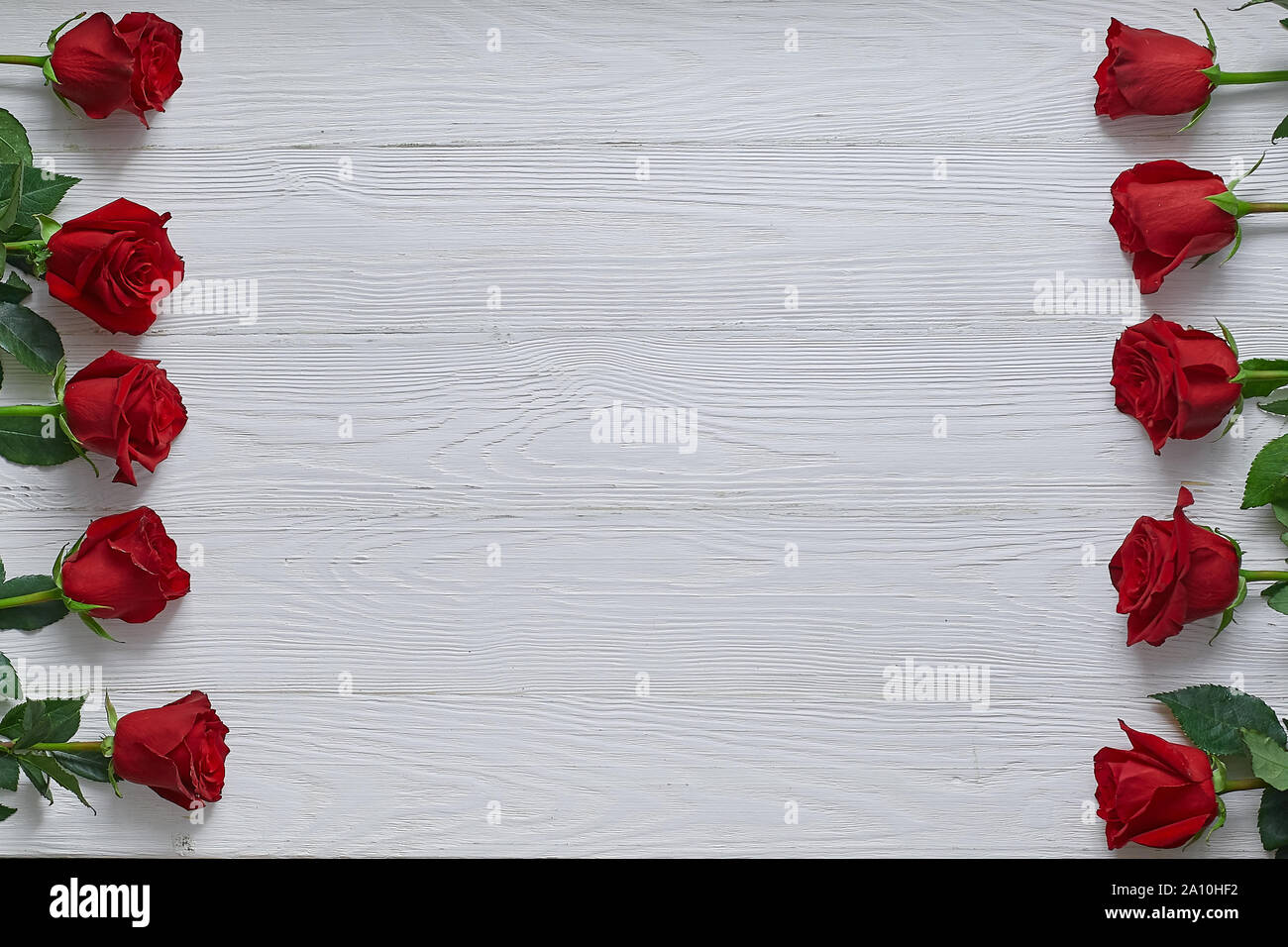 Frame of red roses on white wooden background. With space for text ...