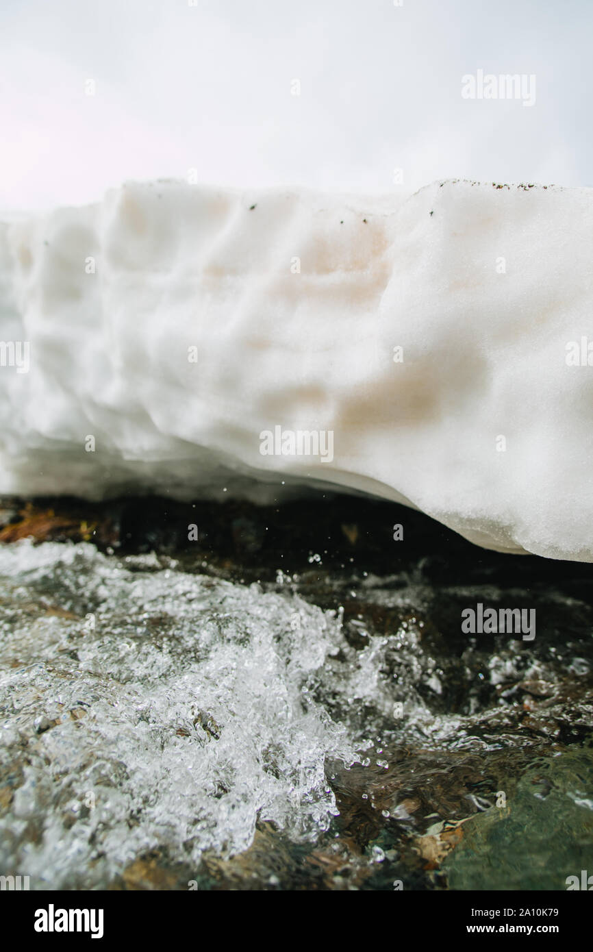 The detailed look at water runs under ice in a river. The snow is ...