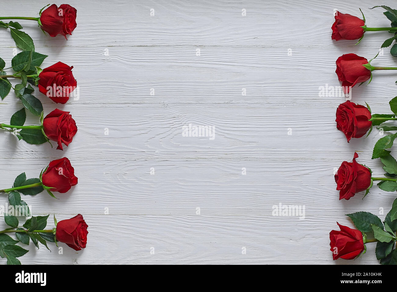Frame of red roses on white wooden background. With space for text ...