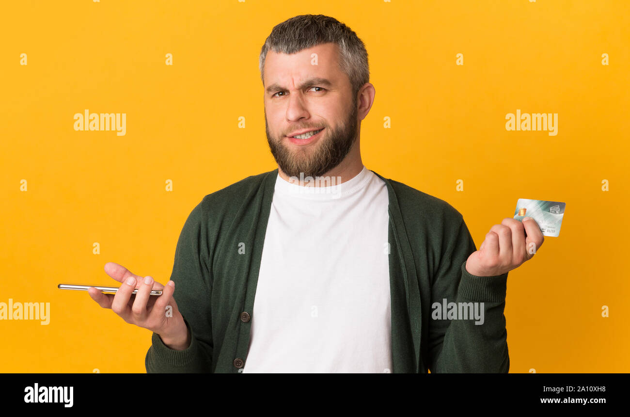 Sceptical man holding cellphone and credit card Stock Photo - Alamy