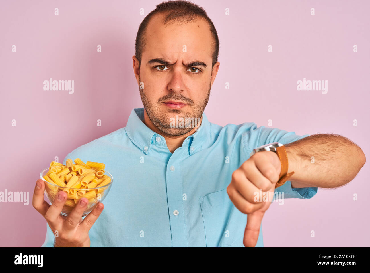 Young man holding bowl with macaroni pasta standing over isolated pink ...