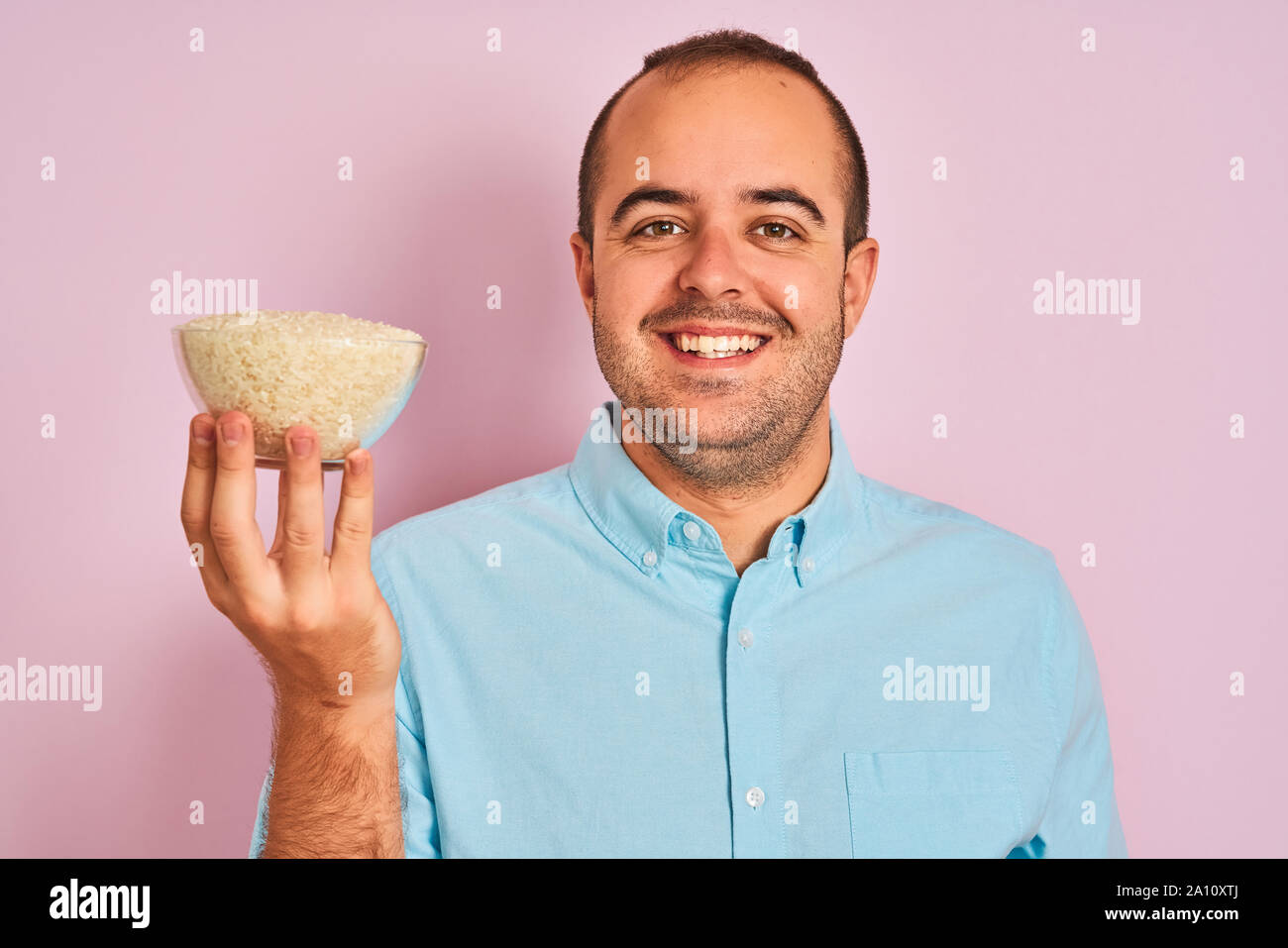 Young man holding bowl with rice standing over isolated pink background ...