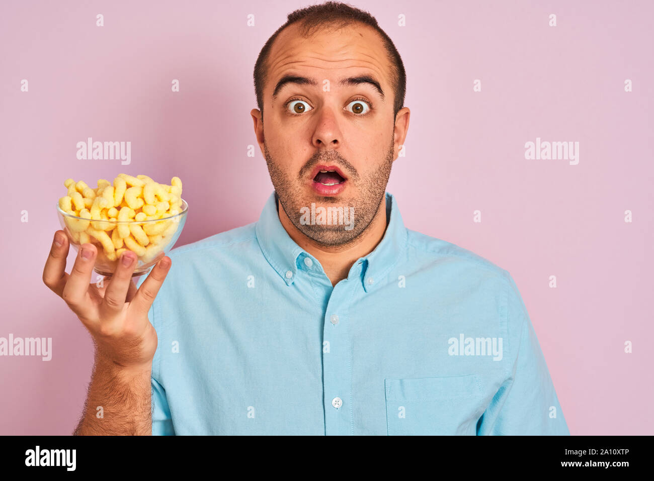 Young man holding bowl with extruded corn standing over isolated pink ...