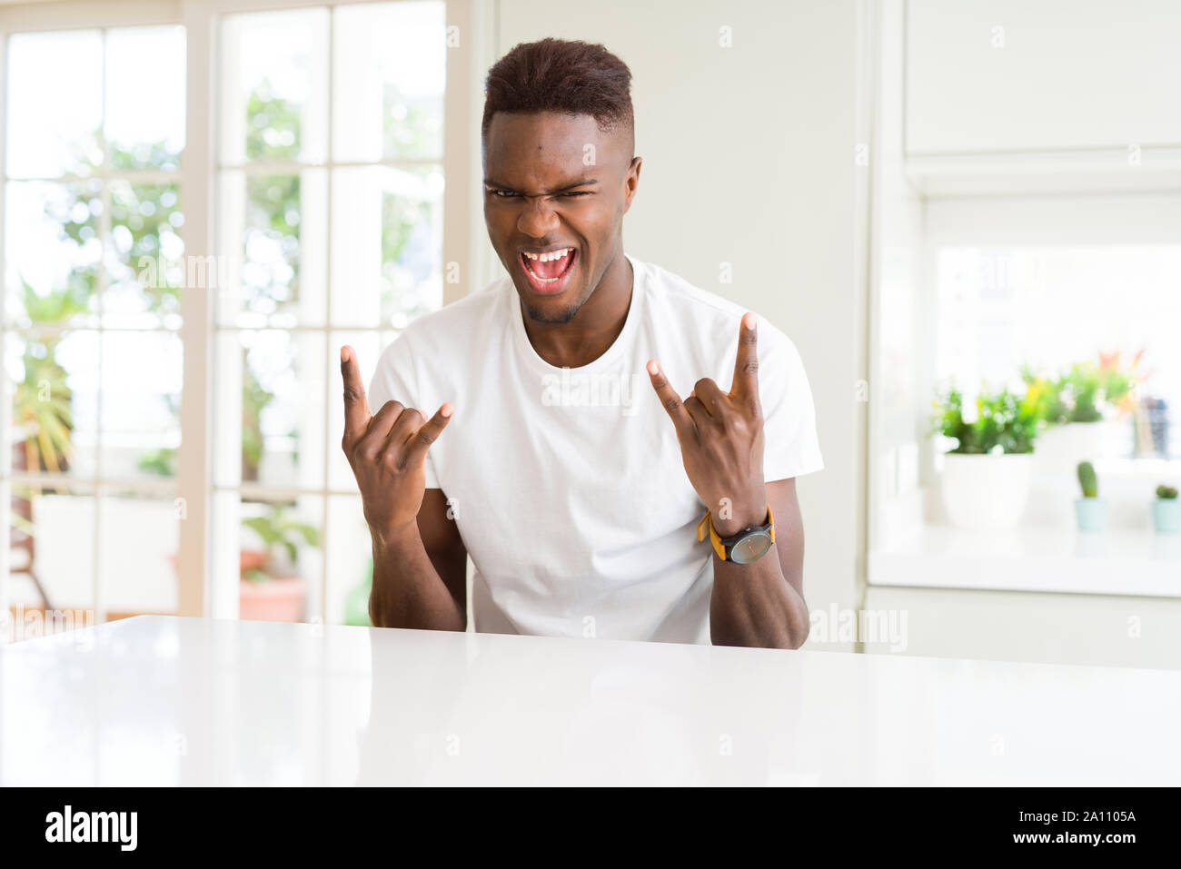 Handsome african american man on white table at home shouting with ...