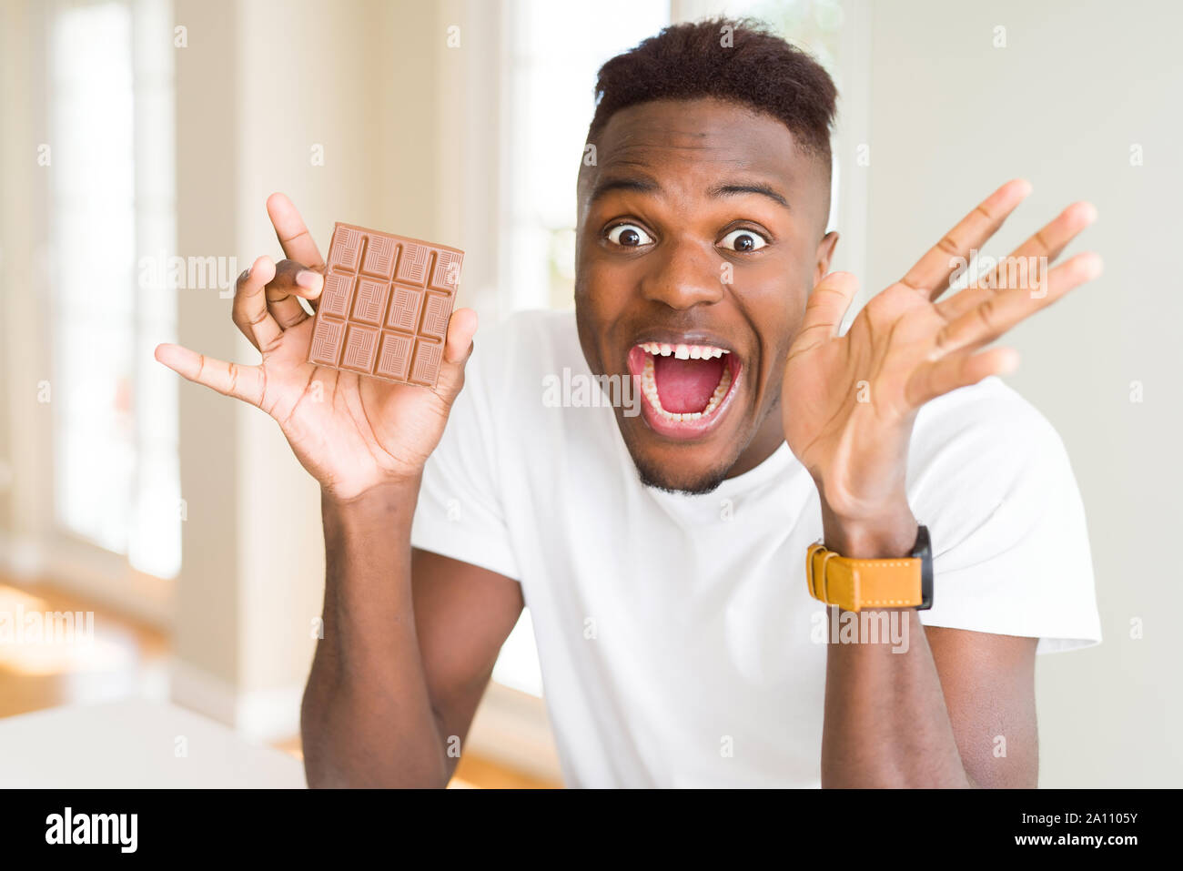 Young african american man eating chocolate bar very happy and excited ...