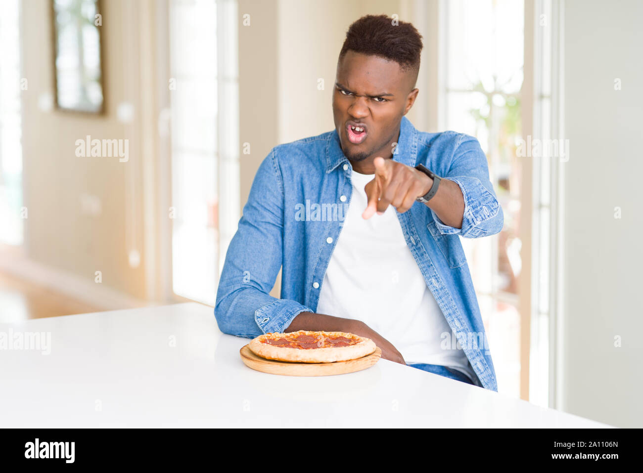 African american man eating pepperoni pizza at home pointing with ...