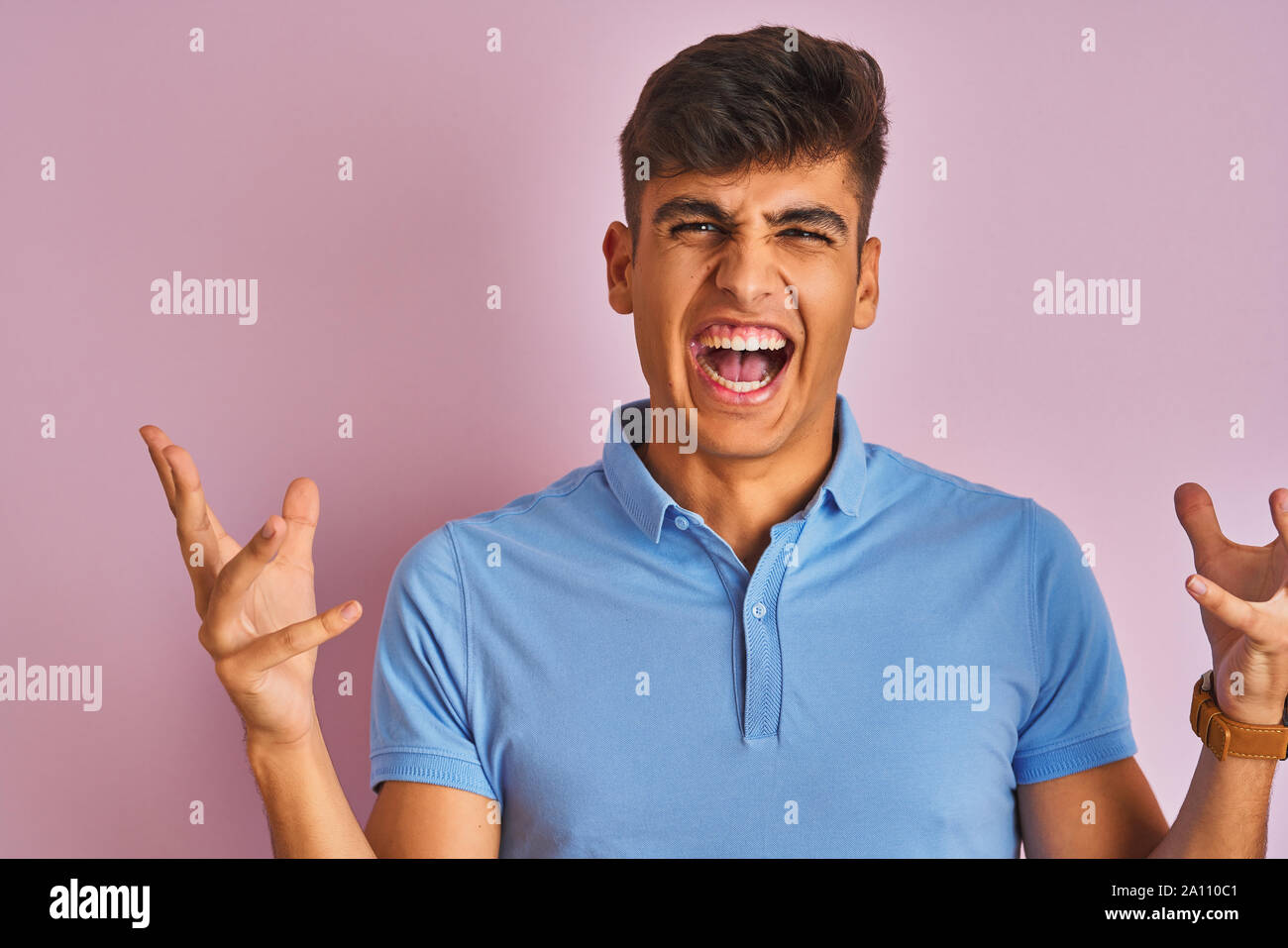 Young indian man wearing blue polo standing over isolated pink ...