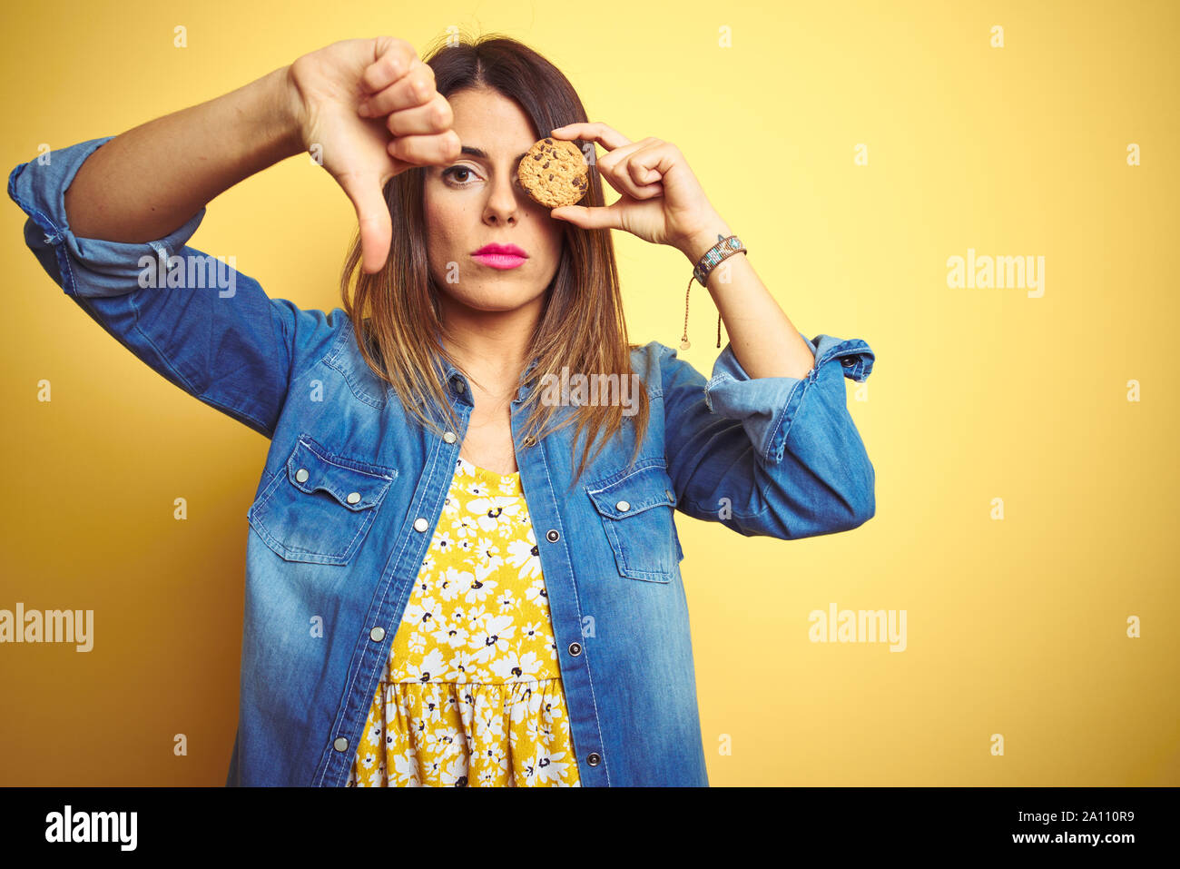 Young beautiful woman eating chocolate chips cookie over yellow ...