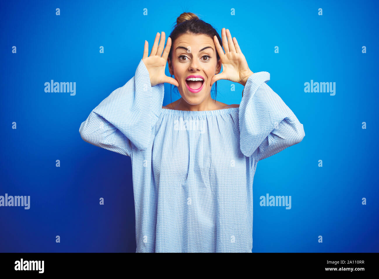 Young beautiful woman wearing bun hairstyle over blue isolated ...