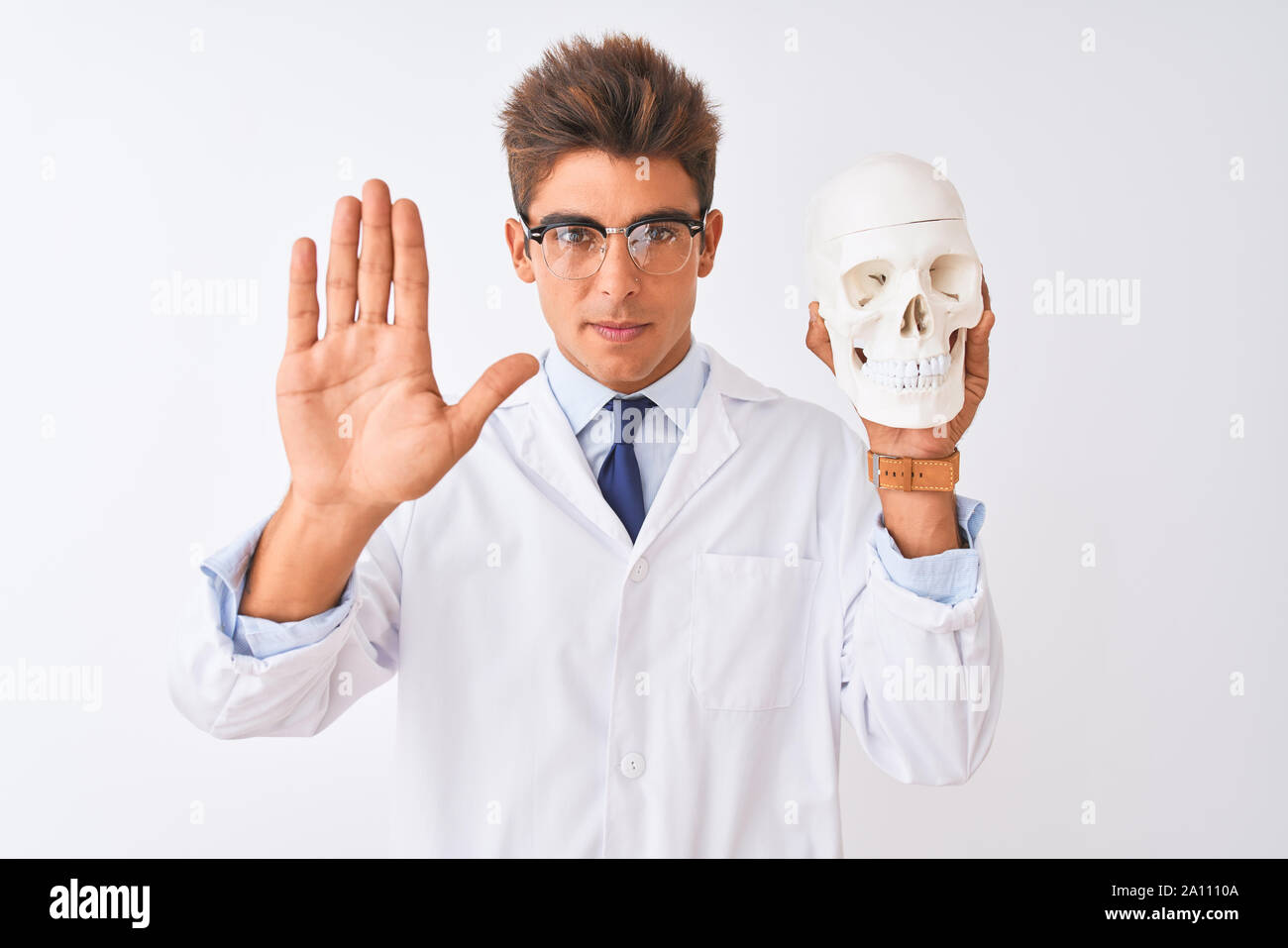 Young handsome doctor man wearing glasses holding skull over isolated ...