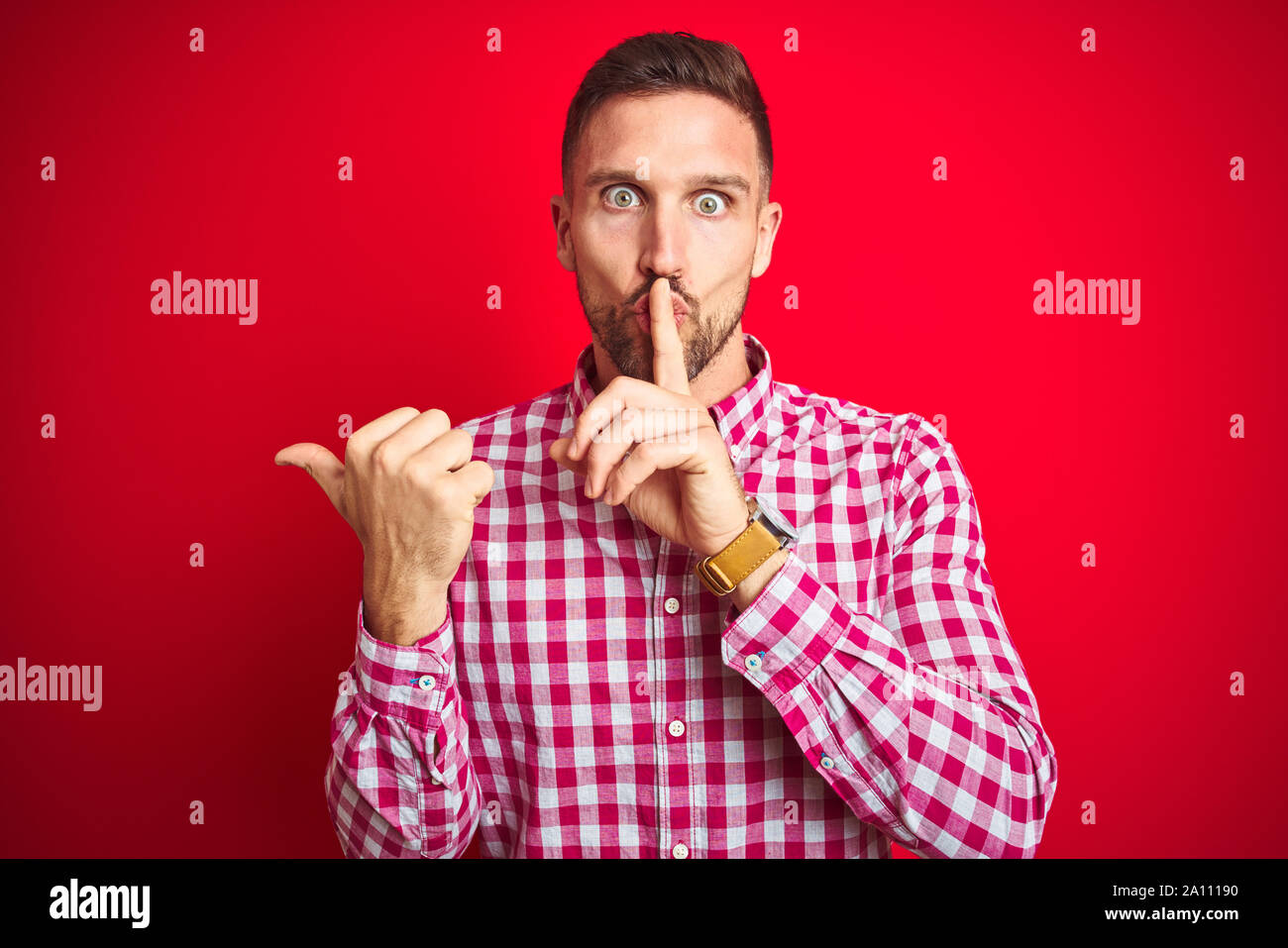 Young handsome man over red isolated background asking to be quiet with ...