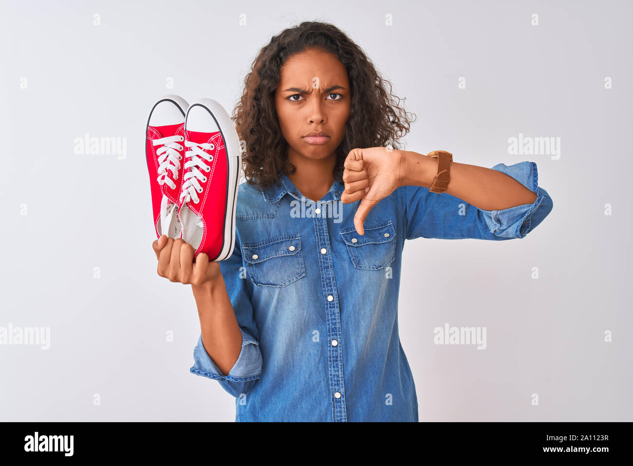 Young brazilian woman holding sneakers standing over isolated white ...