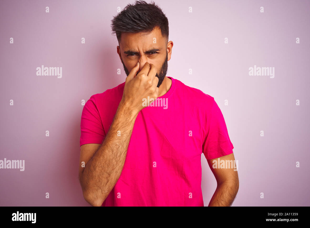 Young indian man wearing t-shirt standing over isolated pink background ...
