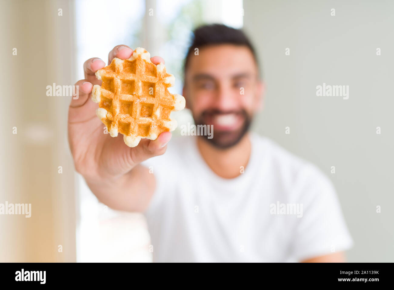 Handsome hispanic man eating sweet belgian waffle pastry with a happy ...