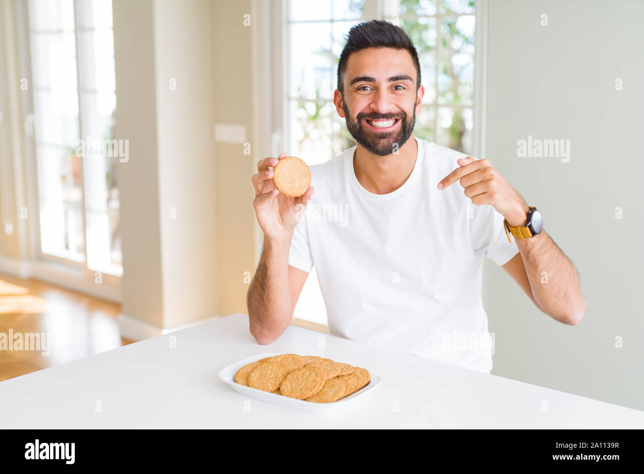Handsome hispanic man eating healthy whole grain biscuits with surprise ...