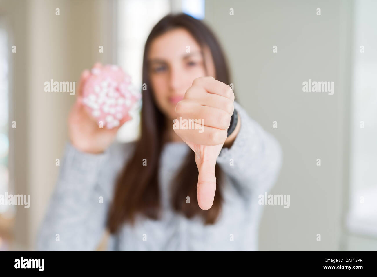 Beautiful young woman eating sugar marshmallow pink donut with angry ...