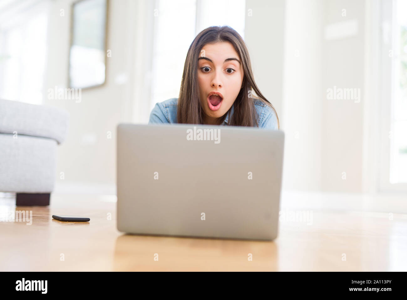 Beautiful young woman laying on the floor using laptop scared in shock ...