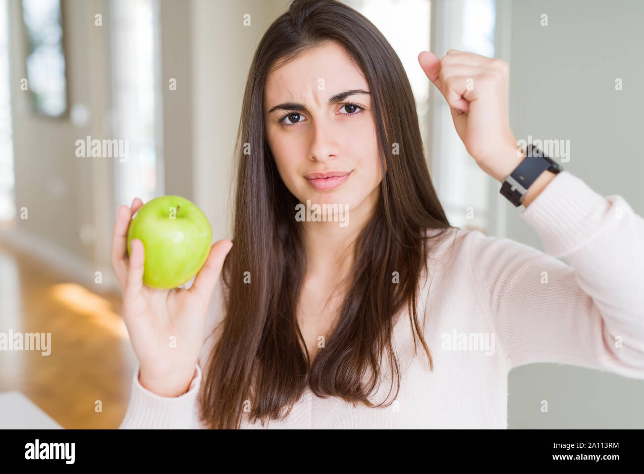 Beautiful young woman eating healthy green apple fruit annoyed and ...