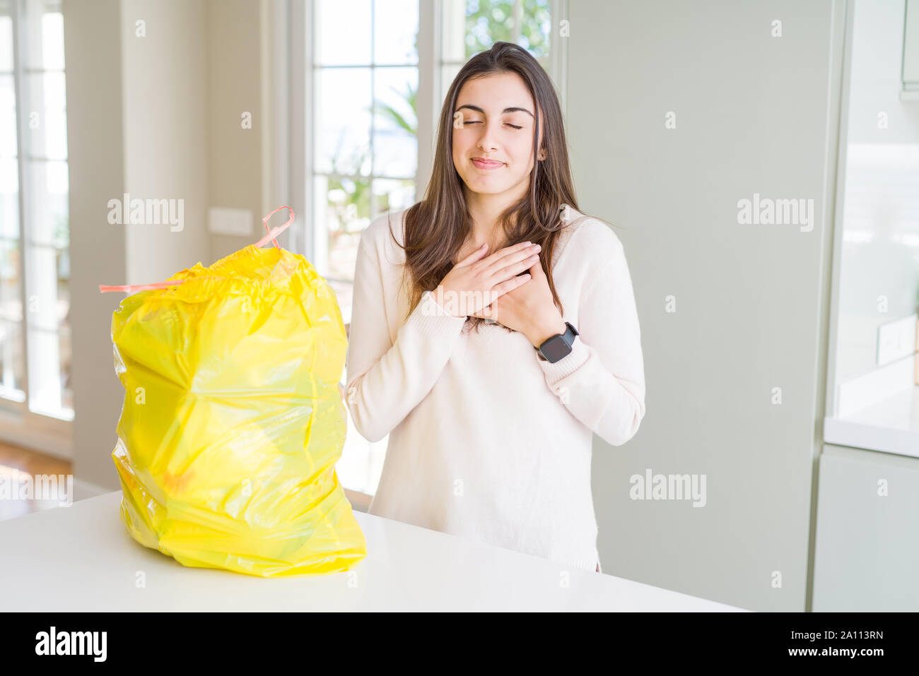 Beautiful young woman taking out the garbage from the rubbish container ...