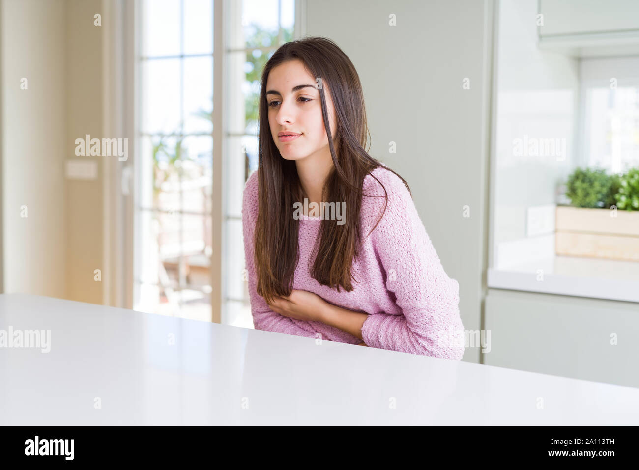 Beautiful young woman wearing pink sweater with hand on stomach because ...