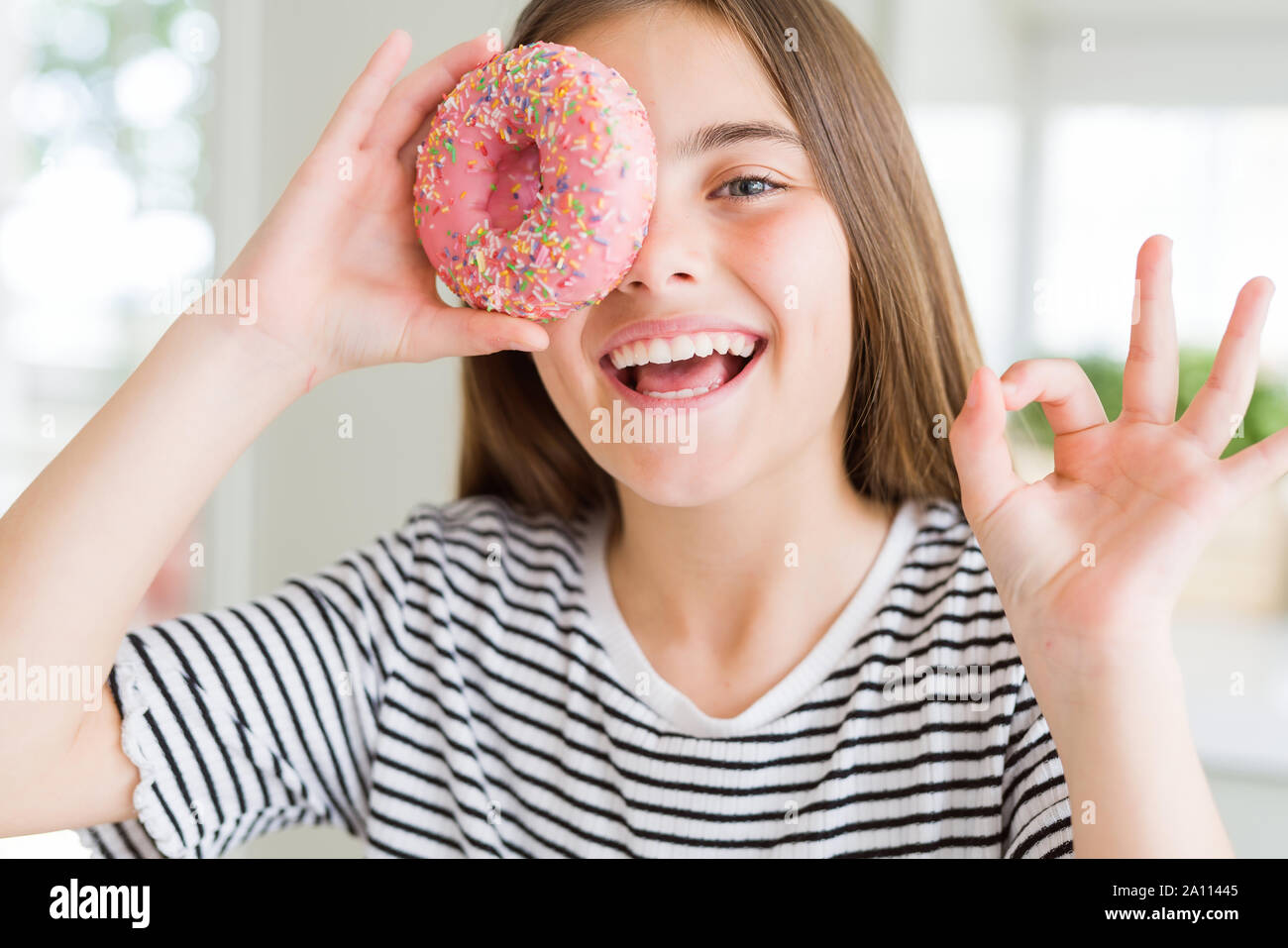 Beautiful young girl kid eating sweet pink donut doing ok sign with ...