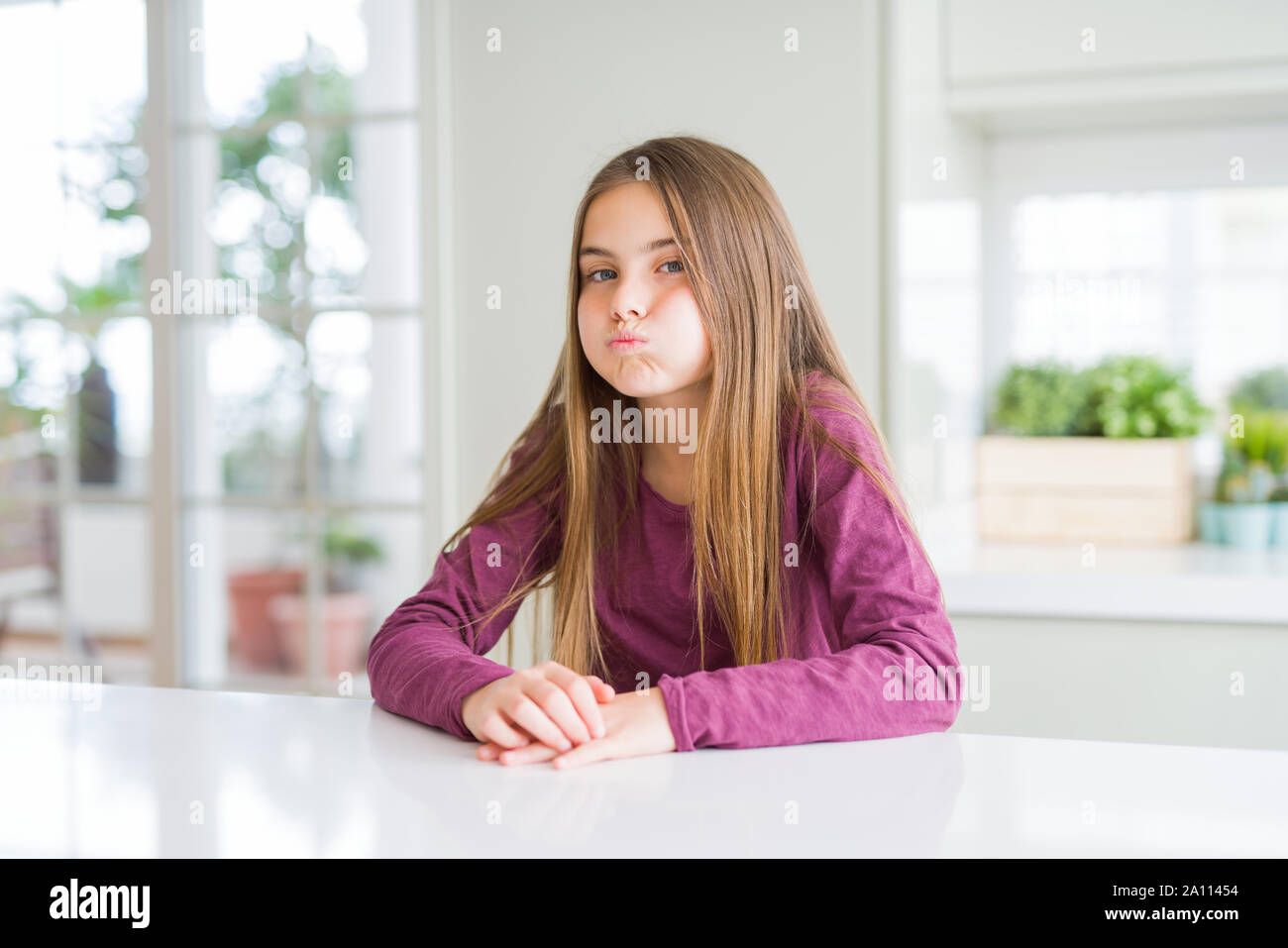 Beautiful young girl kid on white table puffing cheeks with funny face ...
