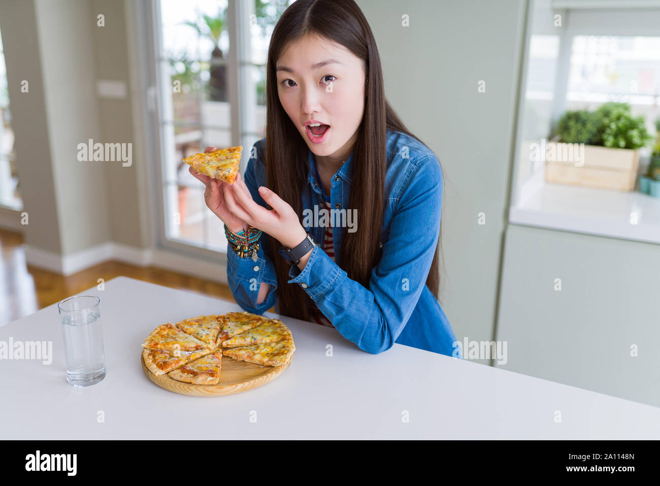 Beautiful Asian woman eating a slice of cheese pizza scared in shock ...