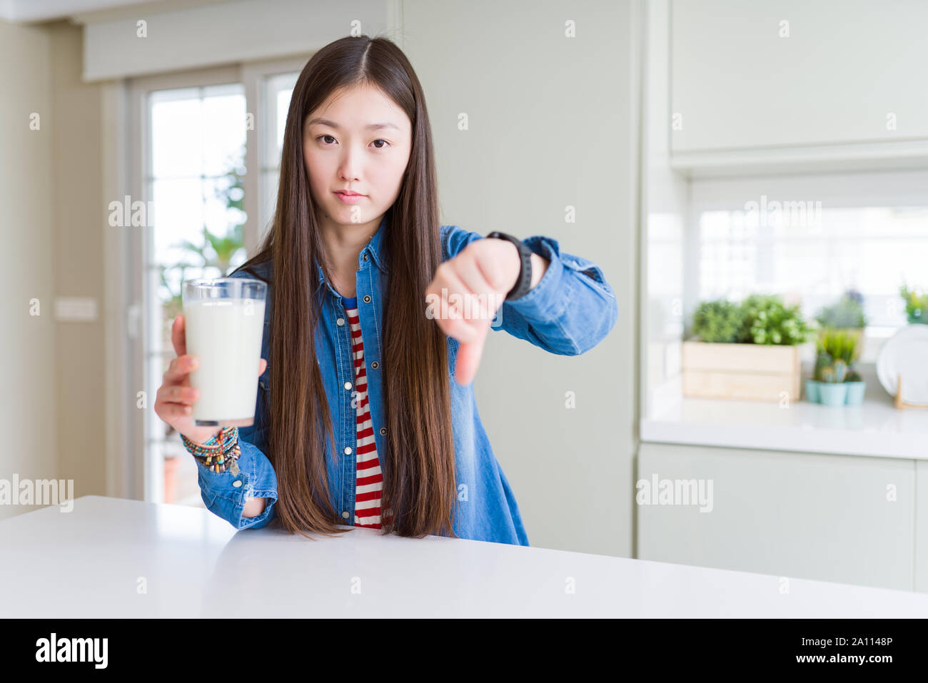 Beautiful Asian woman drinking a fresh glass of milk with angry face ...