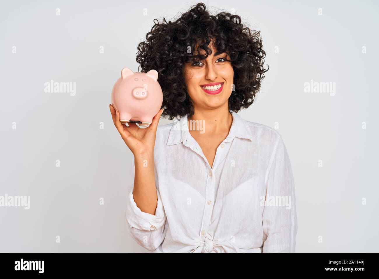 Young arab woman with curly hair holding piggy bank over isolated white ...