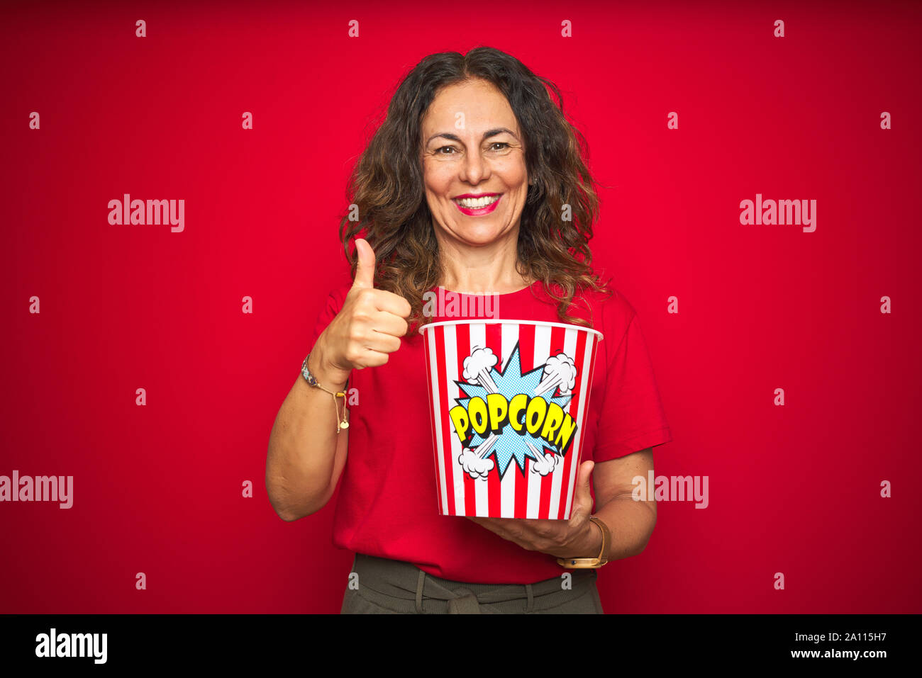 Middle age senior woman eating popcorn snack over red isolated ...