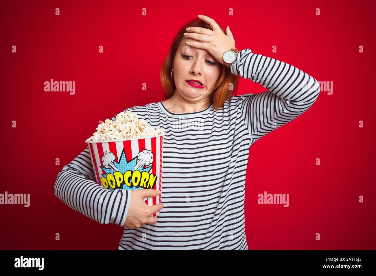 Young beautiful redhead woman eating popcorn over red isolated ...