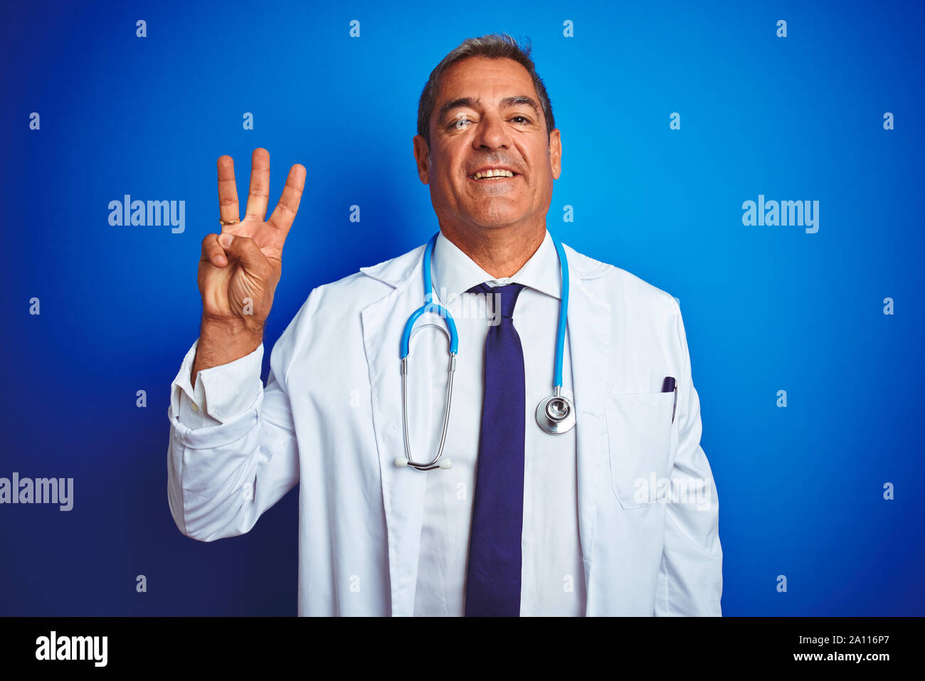 Handsome middle age doctor man wearing stethoscope over isolated blue ...