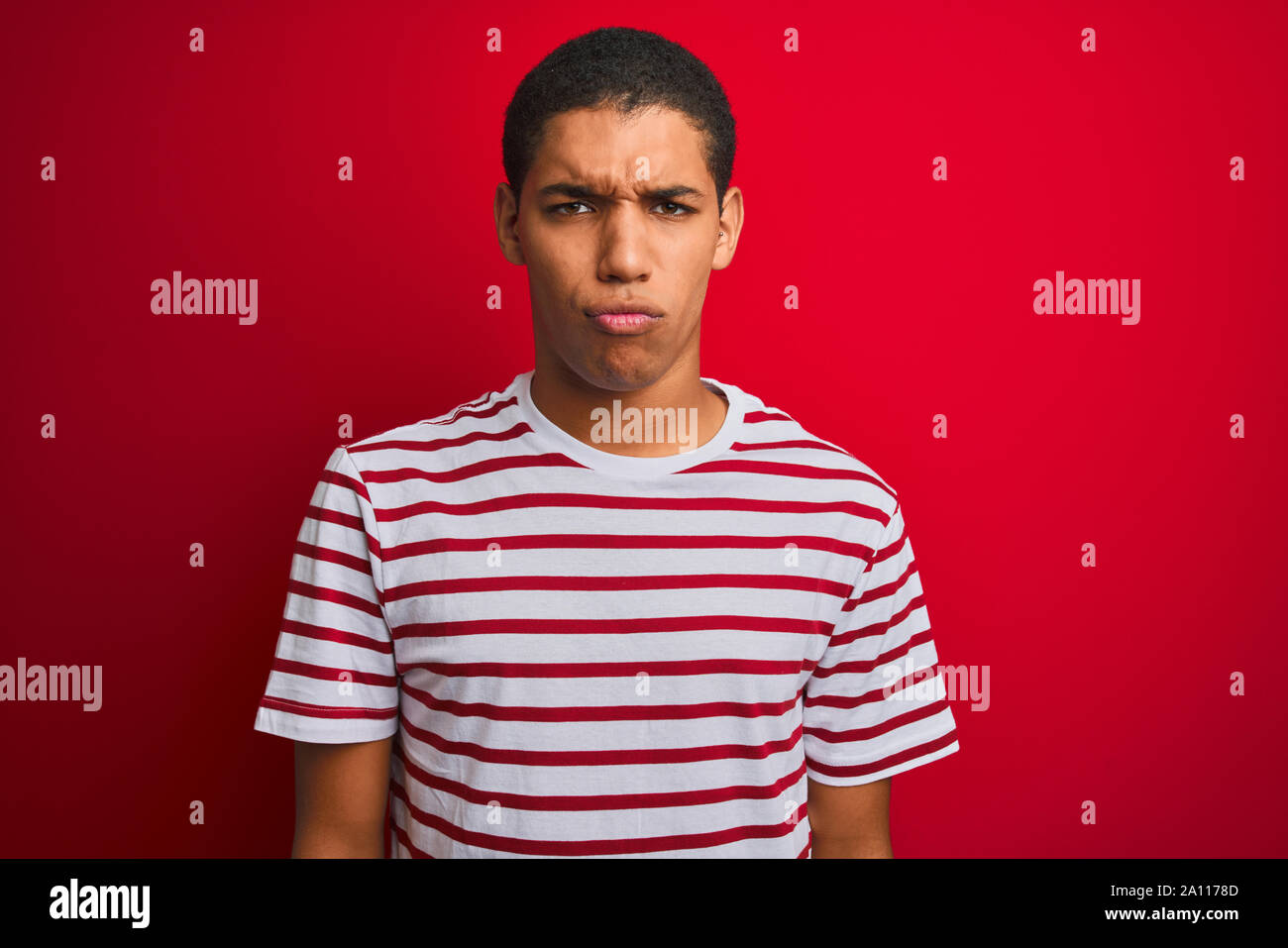 Young handsome arab man wearing striped t-shirt over isolated red ...
