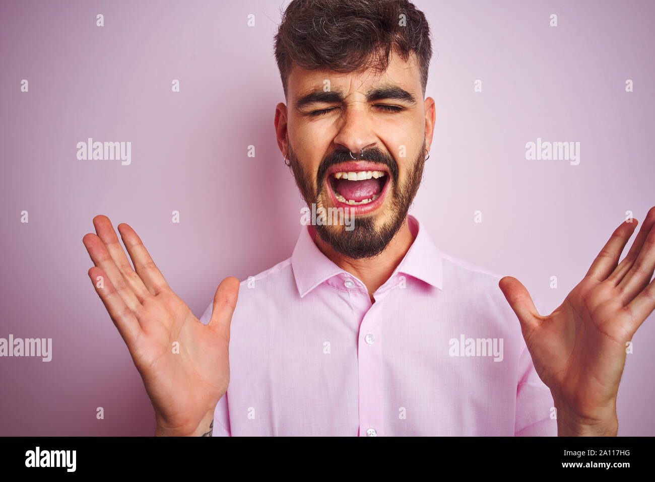 Young man with tattoo wearing shirt standing over isolated pink ...