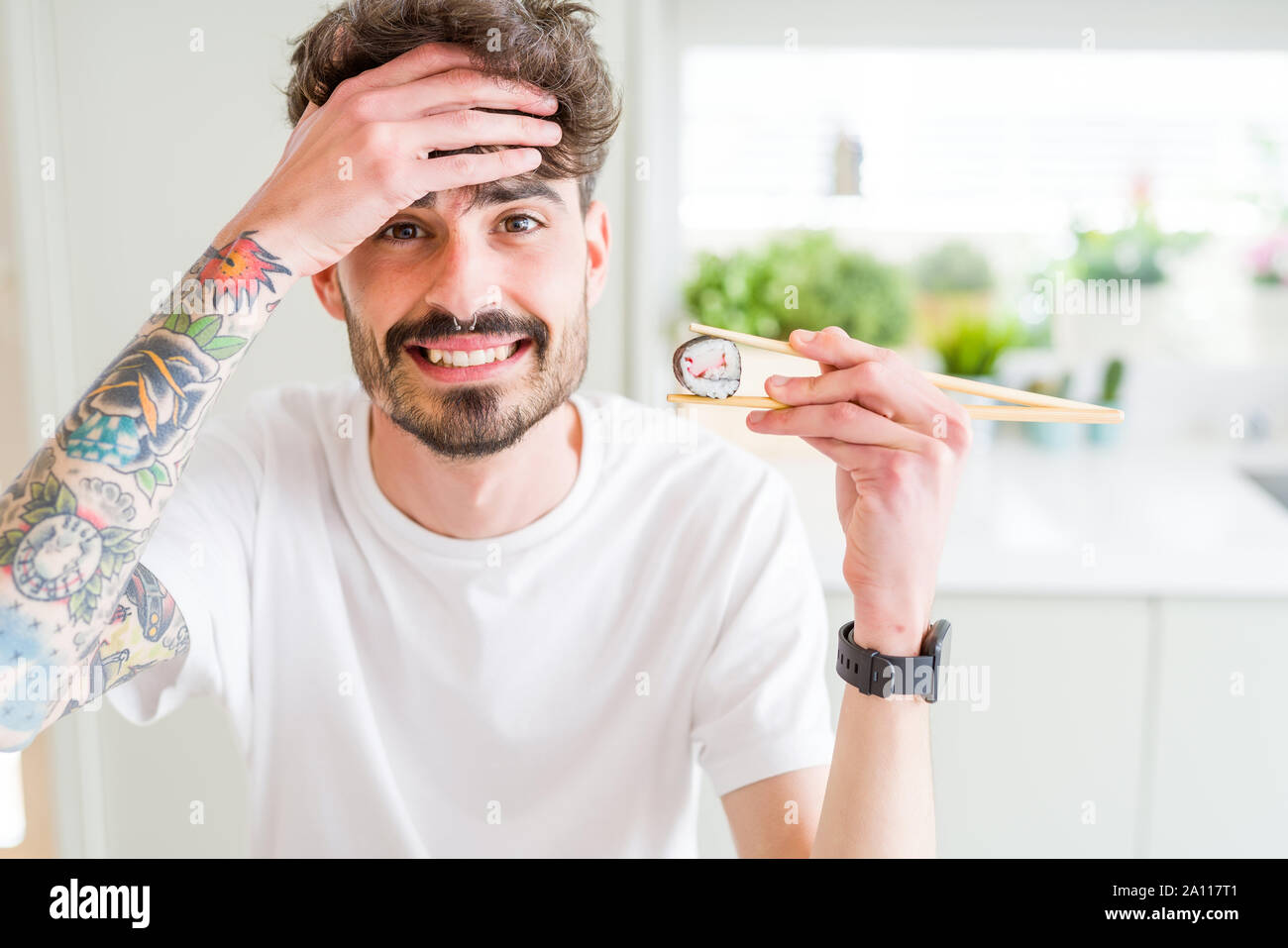 Young man eating asian sushi using chopsticks stressed with hand on ...