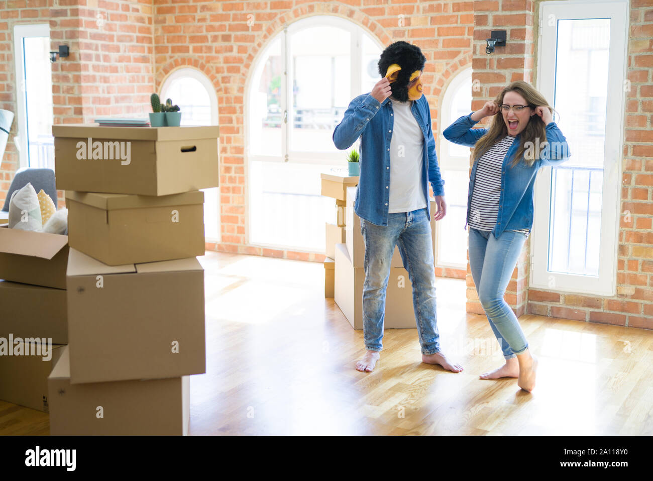 Young couple having fun wearing a monkey mask moving to a new apartment ...