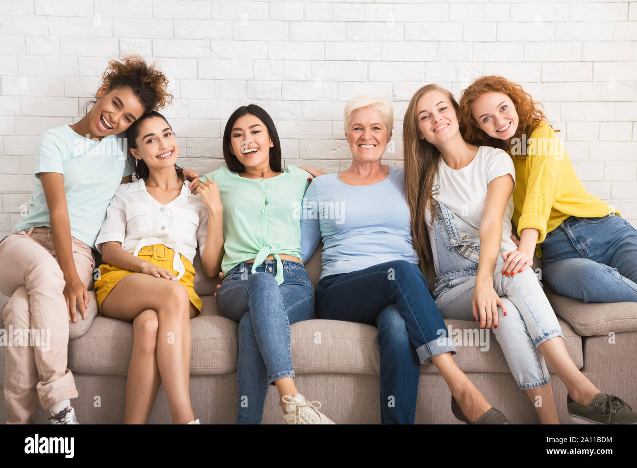 Diverse Women Hugging Sitting On Couch Against White Wall Indoor Stock ...