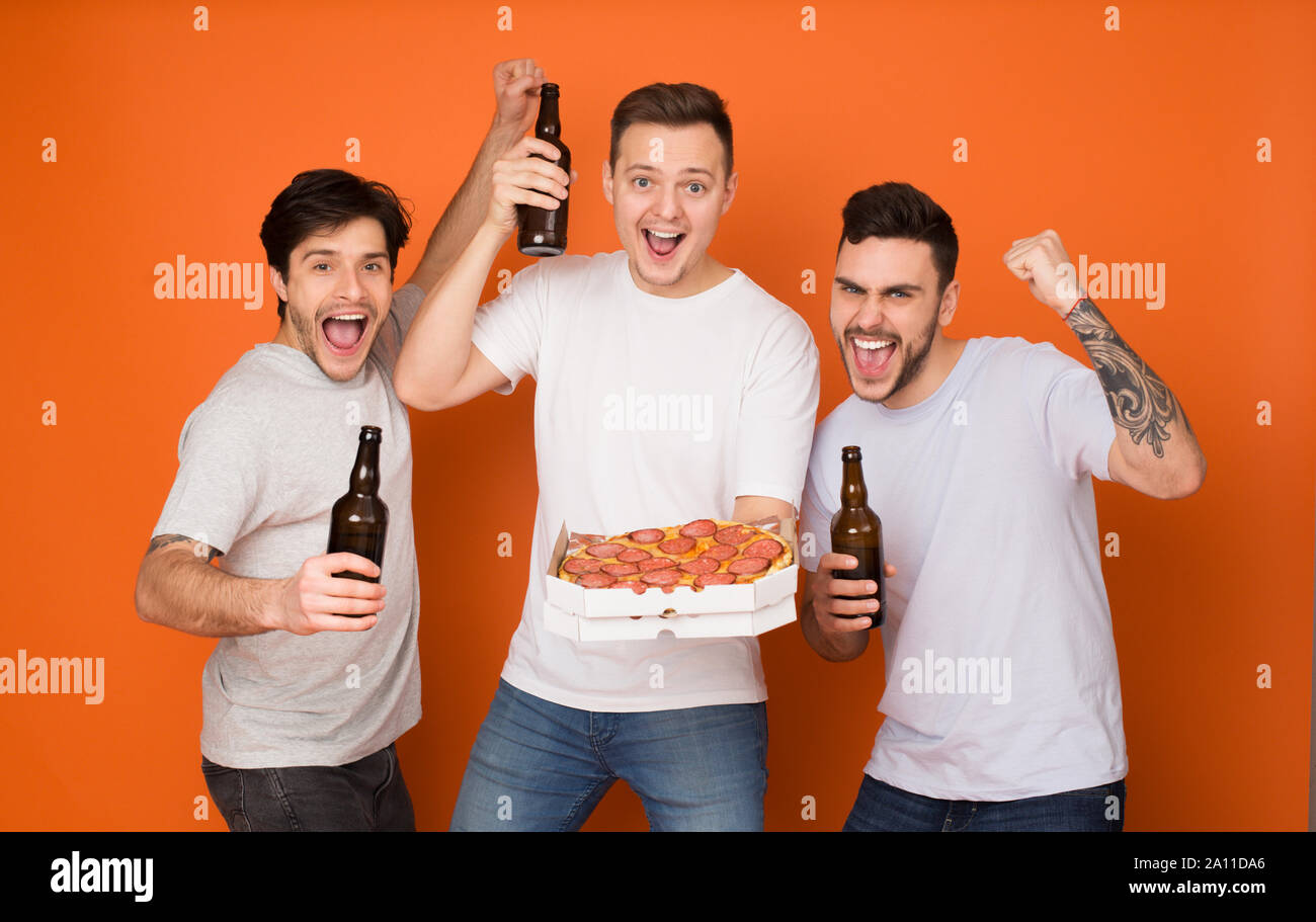 Joyful mates drinking beer and eating pizza, orange background Stock ...