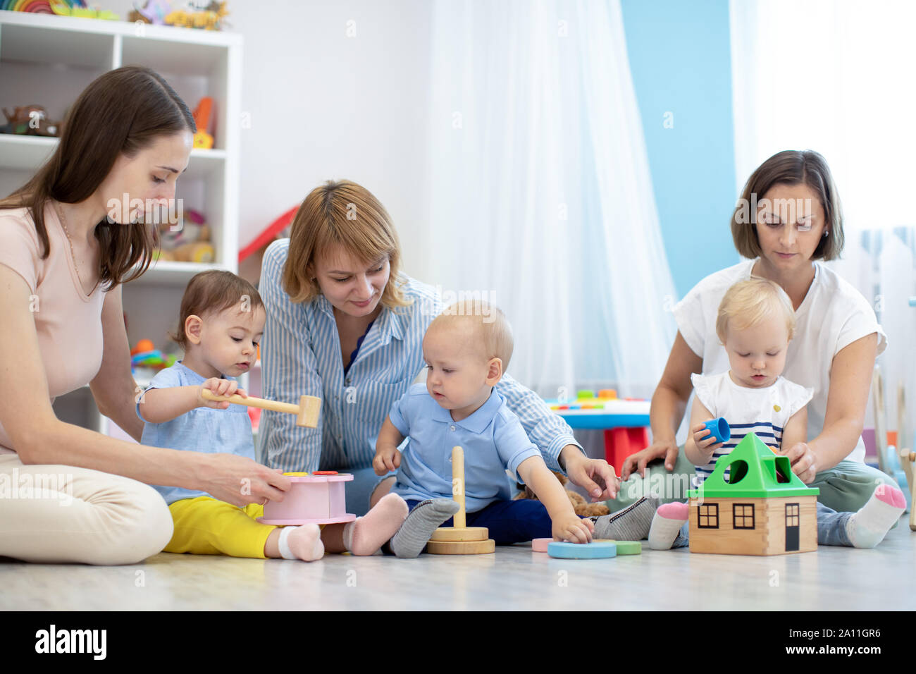 Group of workers with babies in nursery or kindergarten. Moms playing ...