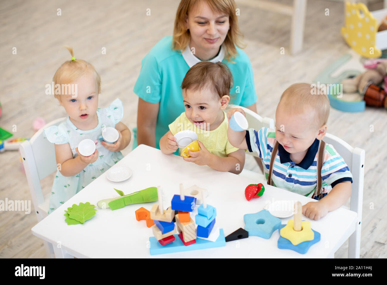 Worker with group of babies in creche. Top view of small kids on lesson ...