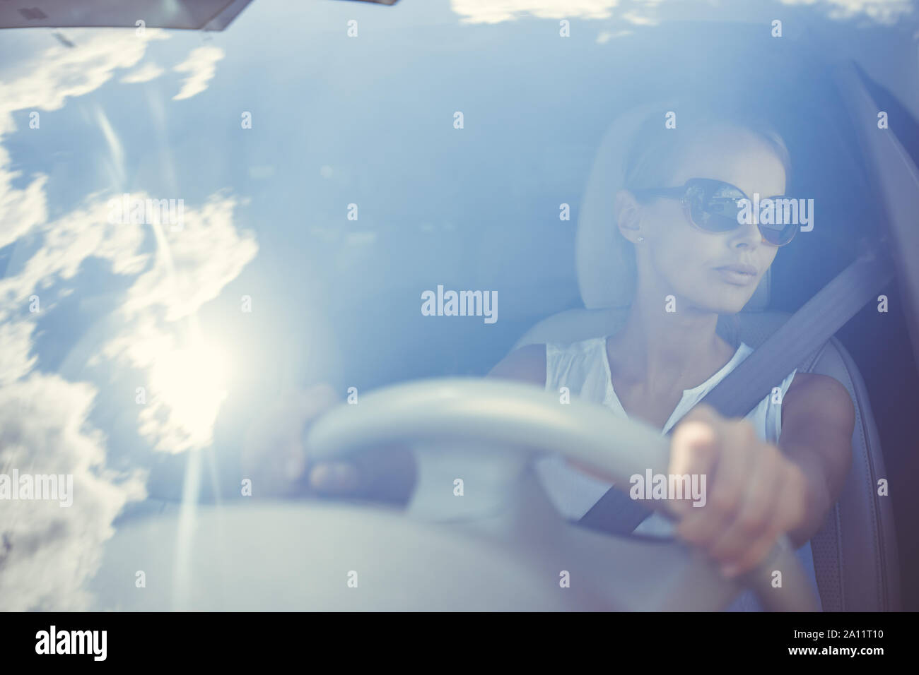 Young female driver driving her car unedr scorching Sun on a hot summer ...