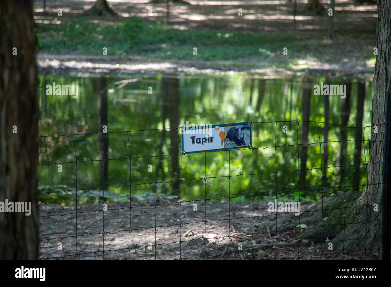 A sign for a tapir with a pond in the background at an enclosure at a ...