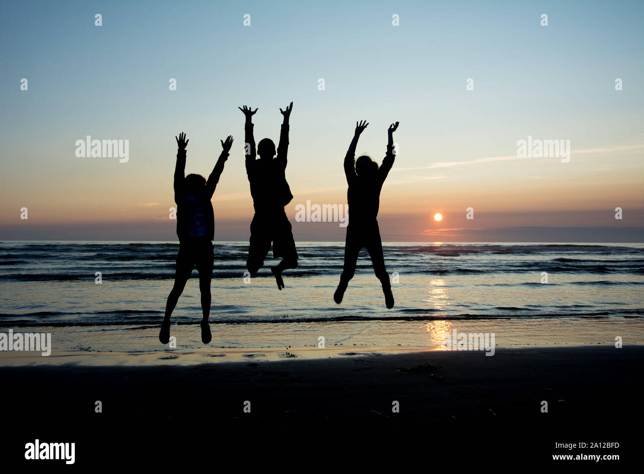 Silhouettes of three teanagers jumping out joyfully on the beach with ...