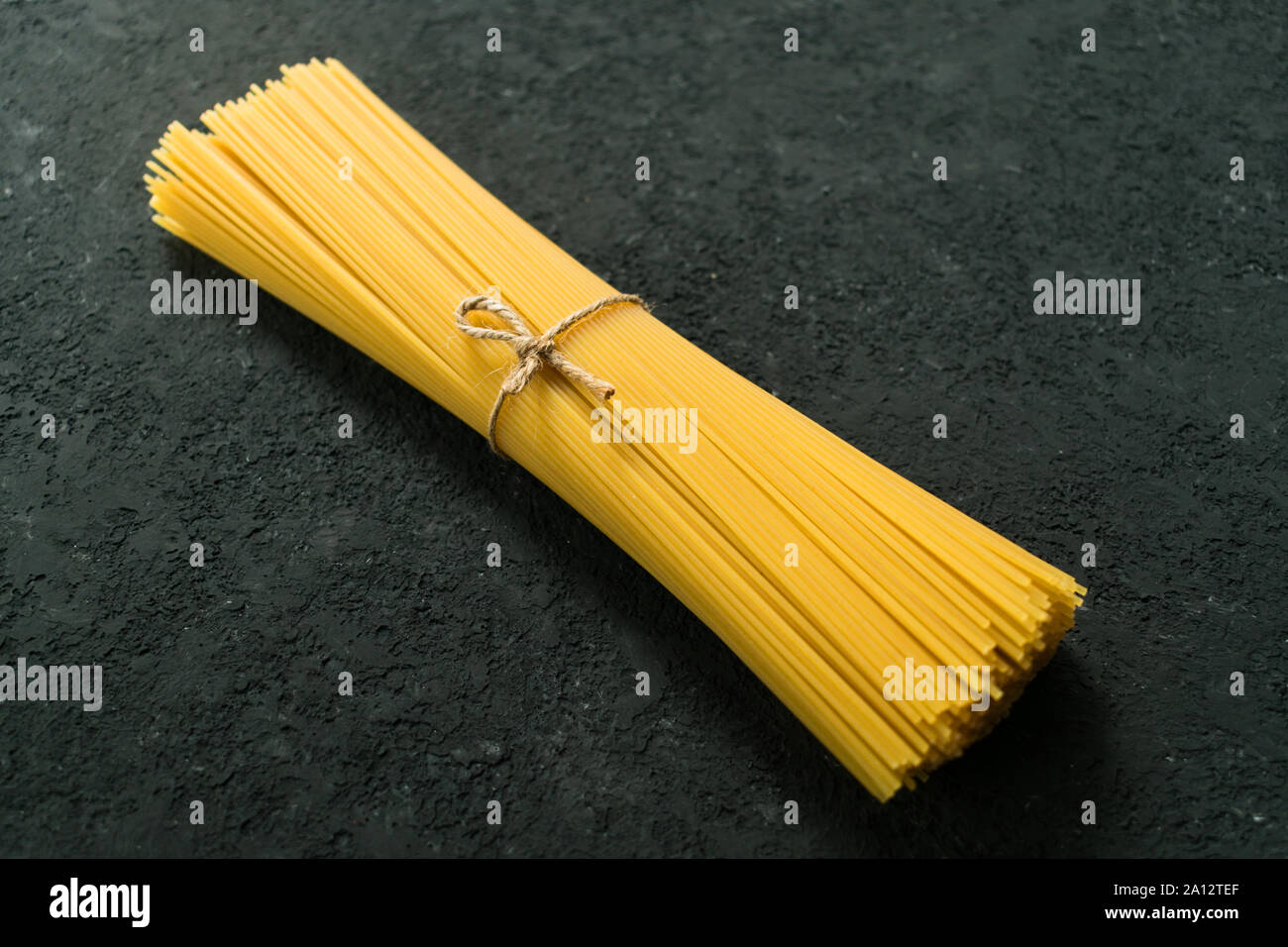 Raw spaghetti pasta tied with a rope on a black texture background ...