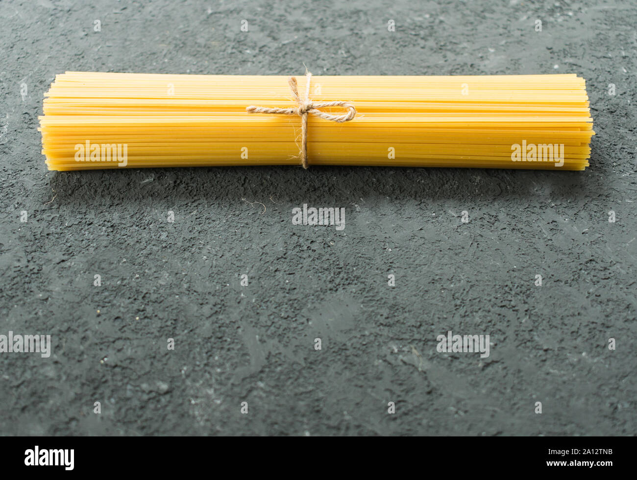 Raw spaghetti pasta tied with a rope on a black texture background ...