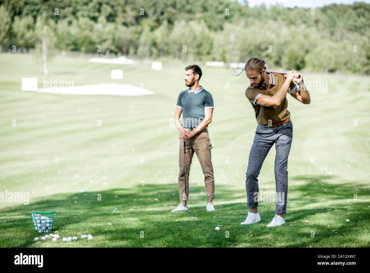 Two male friends playing golf on the golf course, man swinging a putter ...