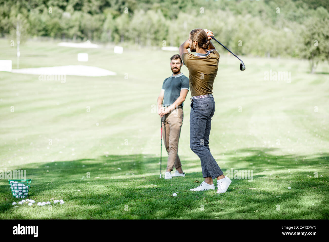Two male friends playing golf on the golf course, man swinging a putter ...