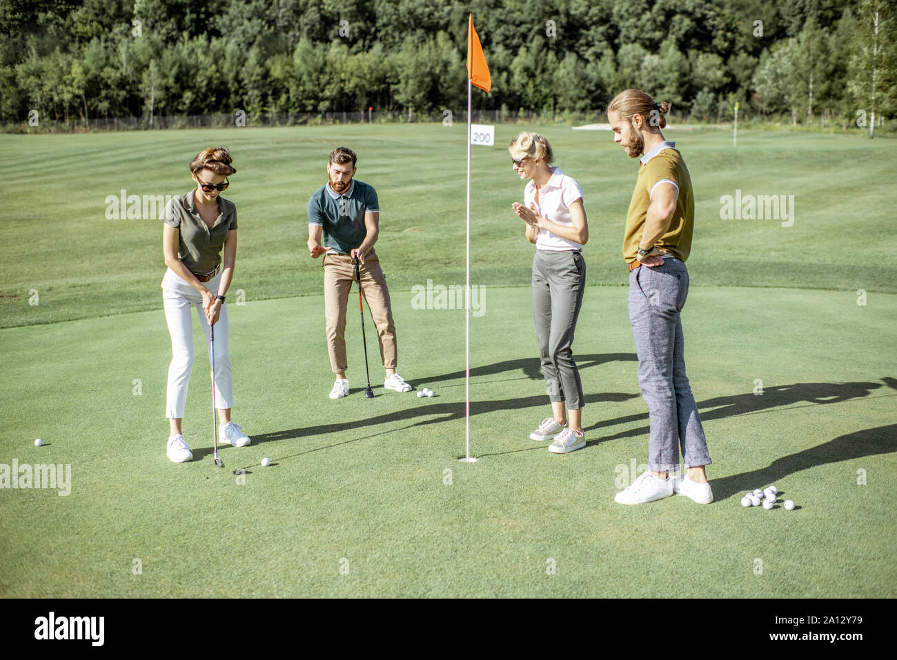 Group of a young friends playing golf, scoring the ball with putter ...